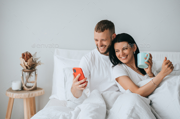 Happy couple in bed making video call by phone, smiling enjoying ...