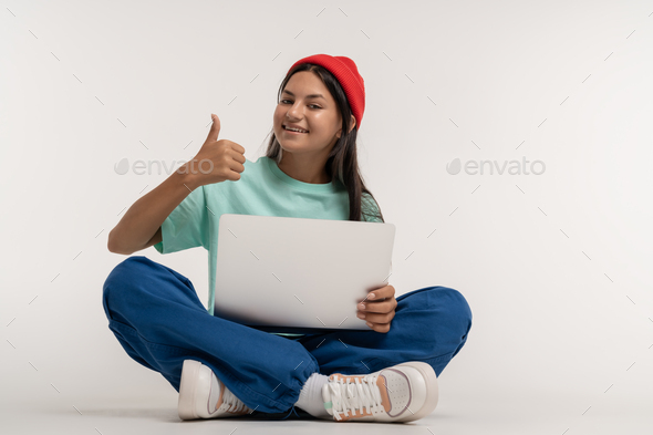 Smiling teenager sitting on floor, showing thumb up gesture expressing ...