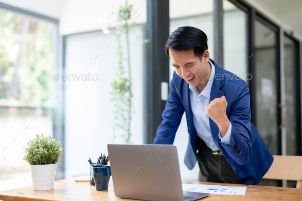 Excited cheerful asian businessman using laptop computer in the office ...