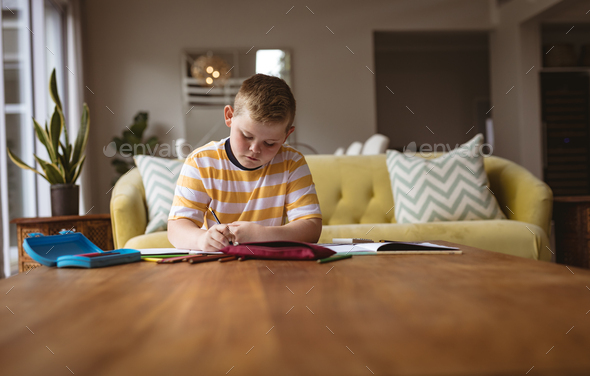 Caucasian boy drawing in his book sitting in the living room at home ...