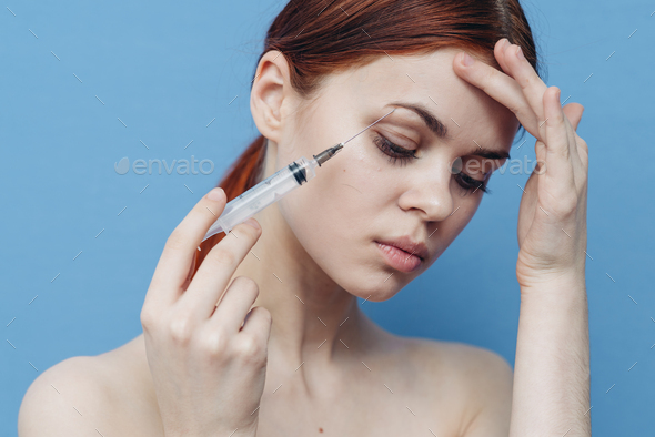woman with a syringe in hand doing injections in the face on a blue ...