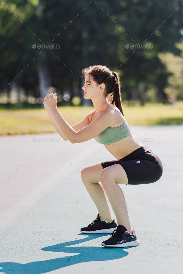 Focused female athlete performs squats at outdoor park, trees in ...