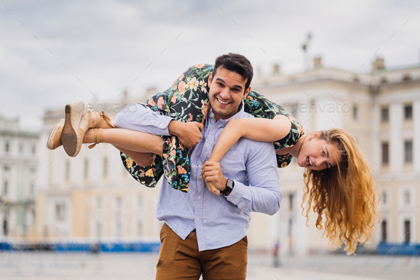 Joyful couple playing piggyback, laughing together in historical square ...