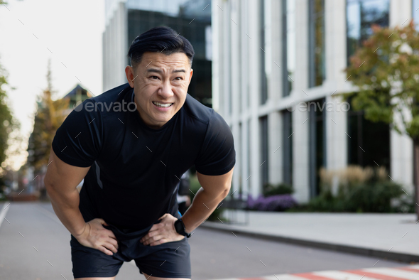 Tired young male athlete stands on the city street at the finish line ...