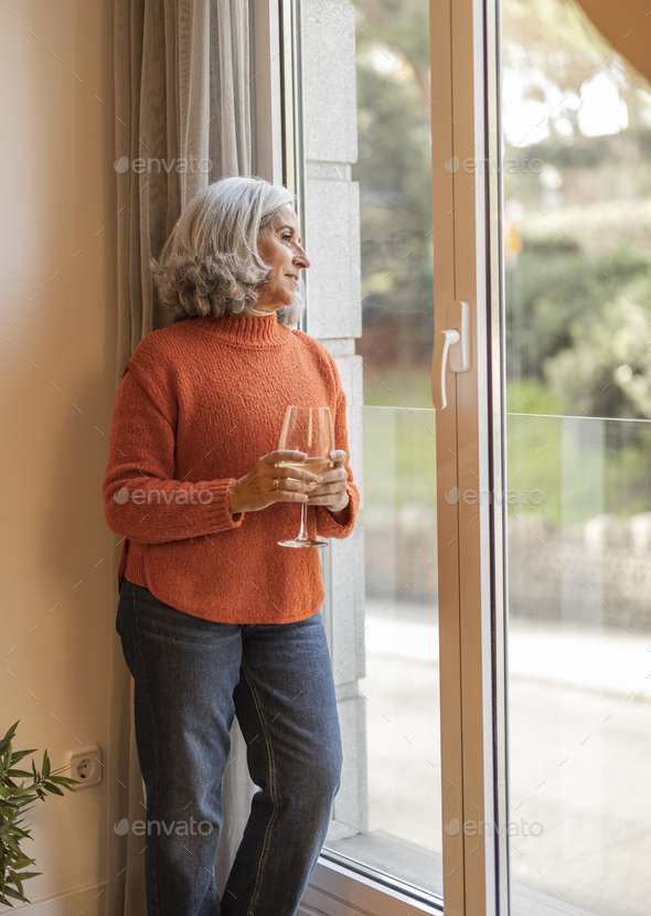 grandmother looking out the window while having a glass waiting for the ...