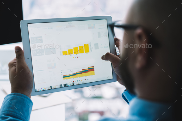 Man looking through charts on tablet Stock Photo by GaudiLab | PhotoDune