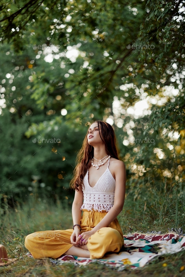 A young hippie woman meditates in nature in the park, sitting in a ...