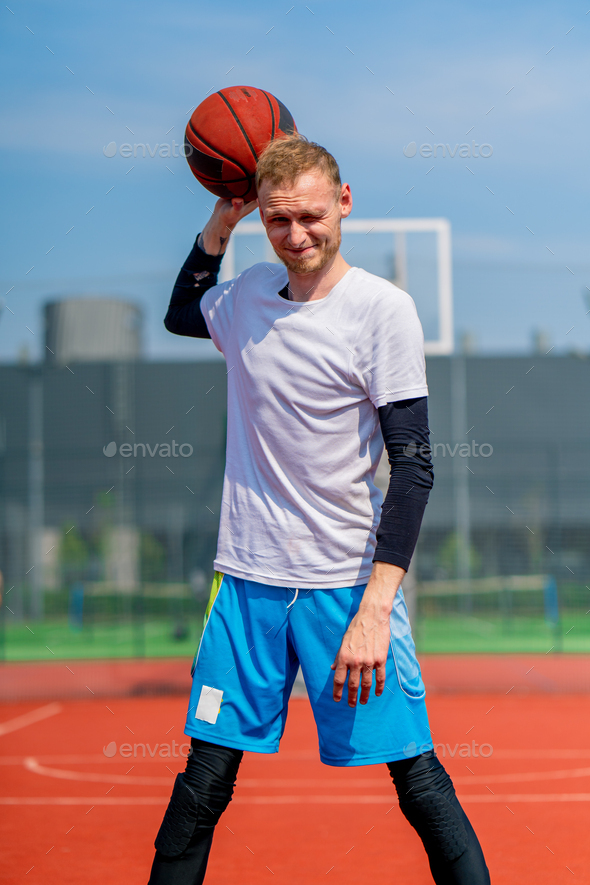 Portrait of a tall guy basketball player holding a ball in his hands on ...