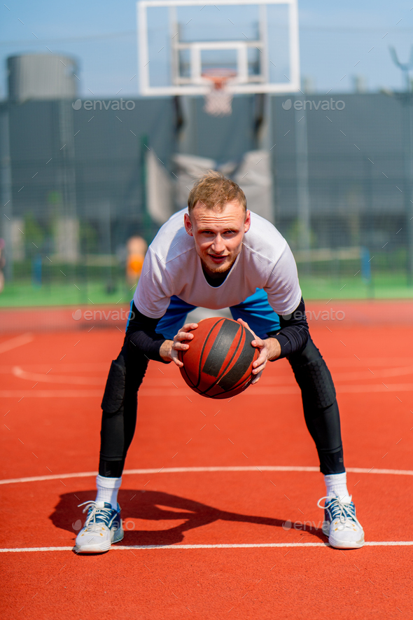 Portrait of a tall guy basketball player holding a ball in his hands on ...
