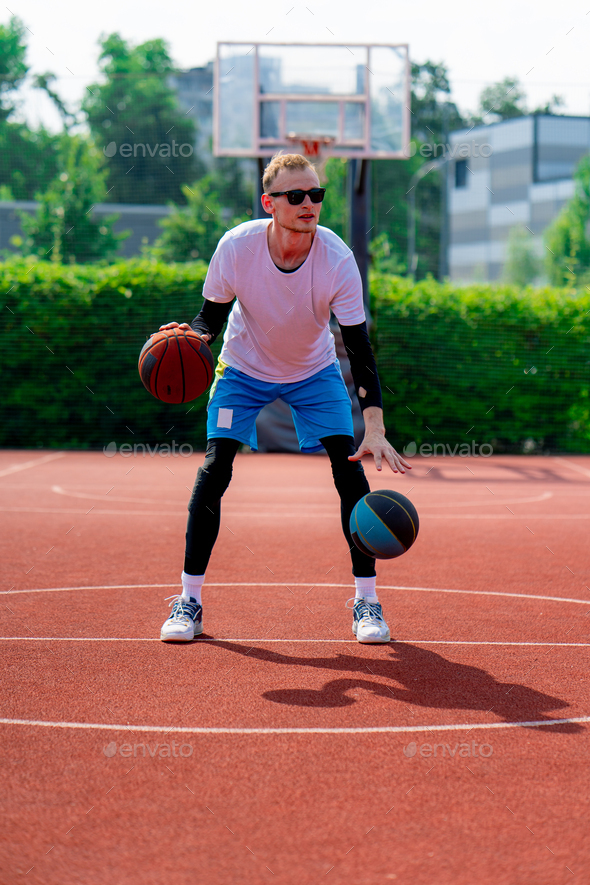 A tall guy basketball player with two balls shows off his dribbling ...