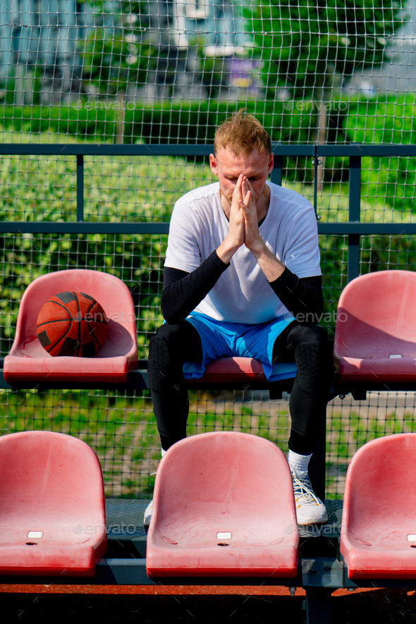 Tall frustrated guy basketball player sitting in the bleachers of a ...