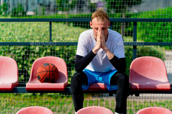 Tall frustrated guy basketball player sitting in the bleachers of a ...