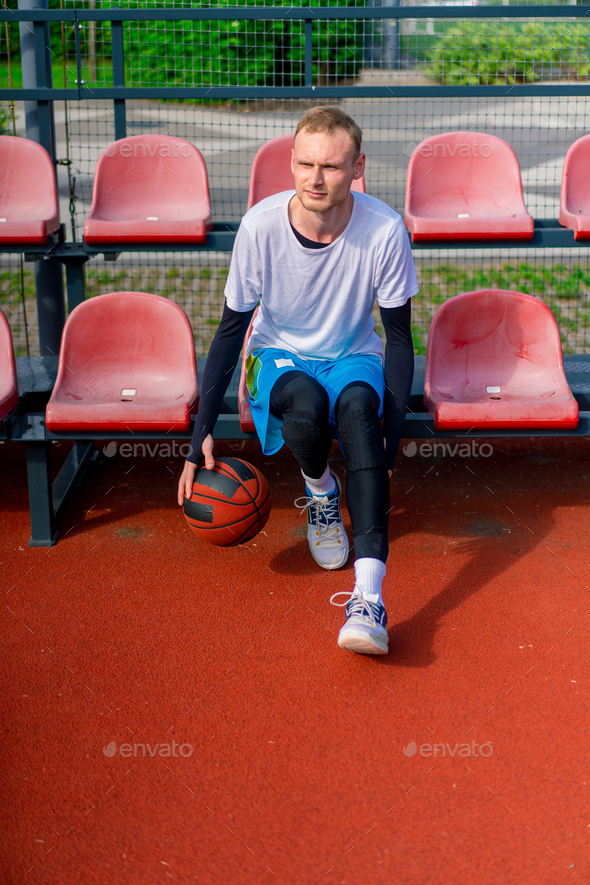 A tall guy basketball player sits in the bleachers an outdoor ...
