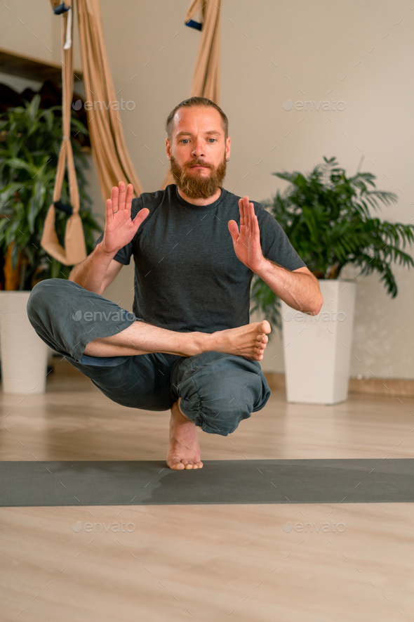 focused adult male yogi with a beard performs a pose exercise from yoga ...
