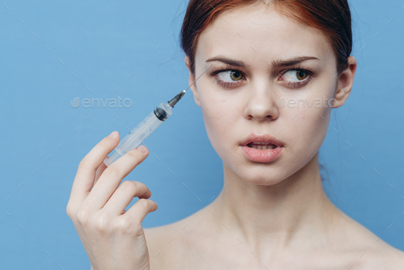 woman with a syringe in hand doing injections in the face on a blue ...