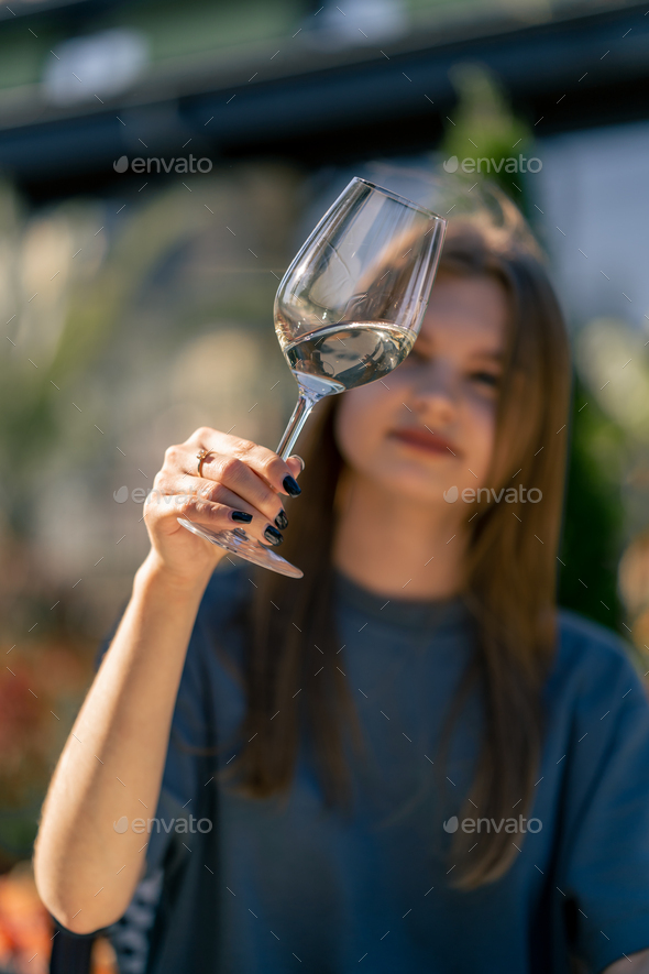 girl holding a glass of wine in her hand inhaling its aroma and tasting ...