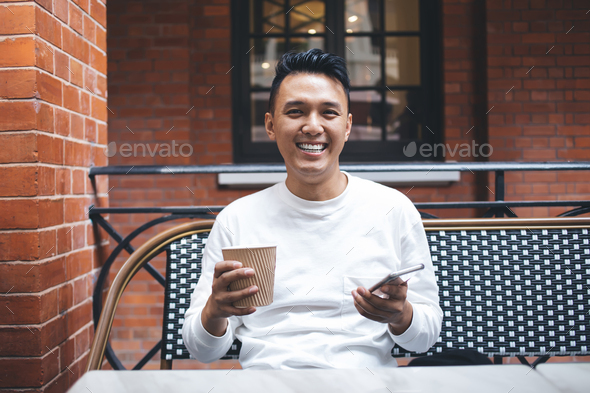 Happy young ethnic male student using phone and holding drink Stock ...
