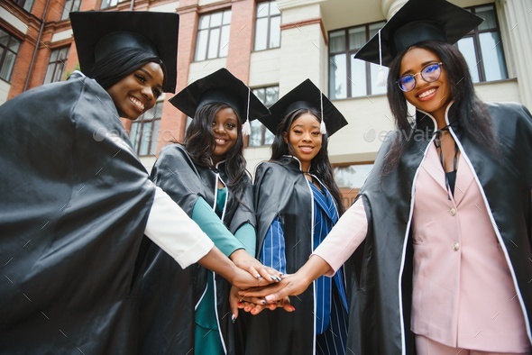 young graduates standing in front of university building on graduation ...