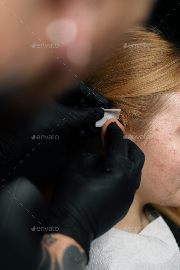 Piercing studio master treats the girl's ear with an antiseptic before ...