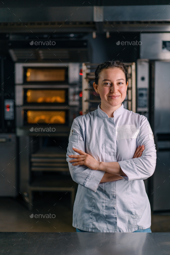 smiling beautiful woman baker in uniform stands near the oven before ...