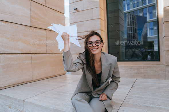 Content businesswoman with glasses sits on steps, playfully waving ...