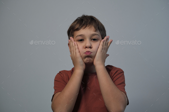 Boy puffing cheeks, hands framing face; a playful gesture. Captures the ...