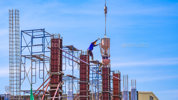 2 construction workers on scaffolding are pouring concrete into column ...
