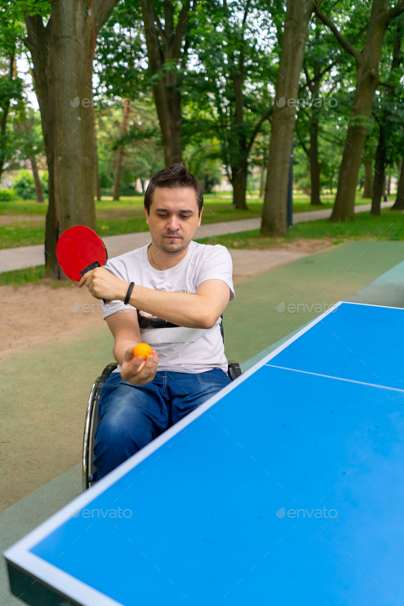 A disabled man in a wheelchair plays ping pong in a city park against ...