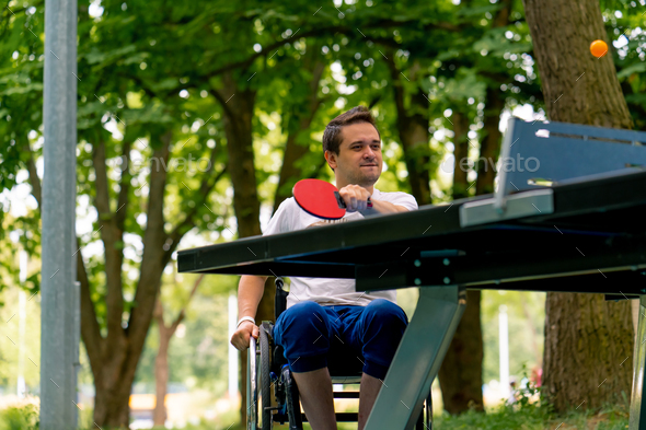 A disabled man in a wheelchair plays ping pong in a city park against ...