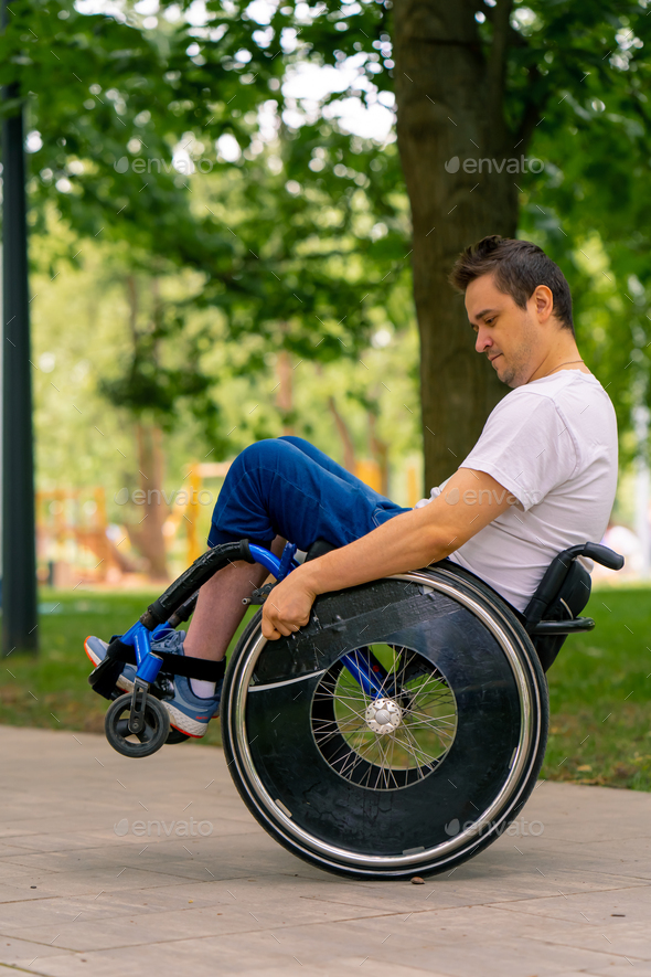 A man with a disability does wheelchair stunts in a city park against ...