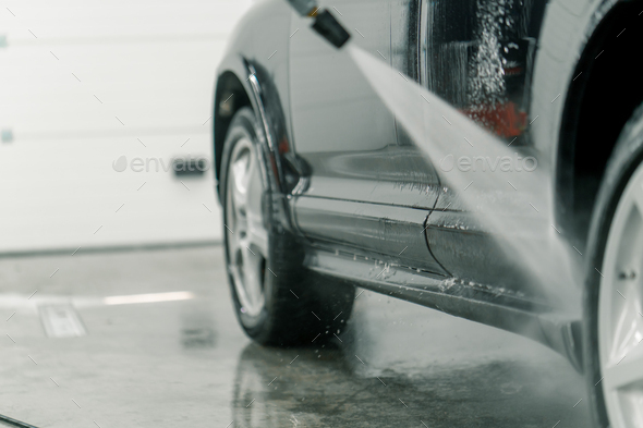Close-up of a male car wash employee washing the sills of rims a black ...