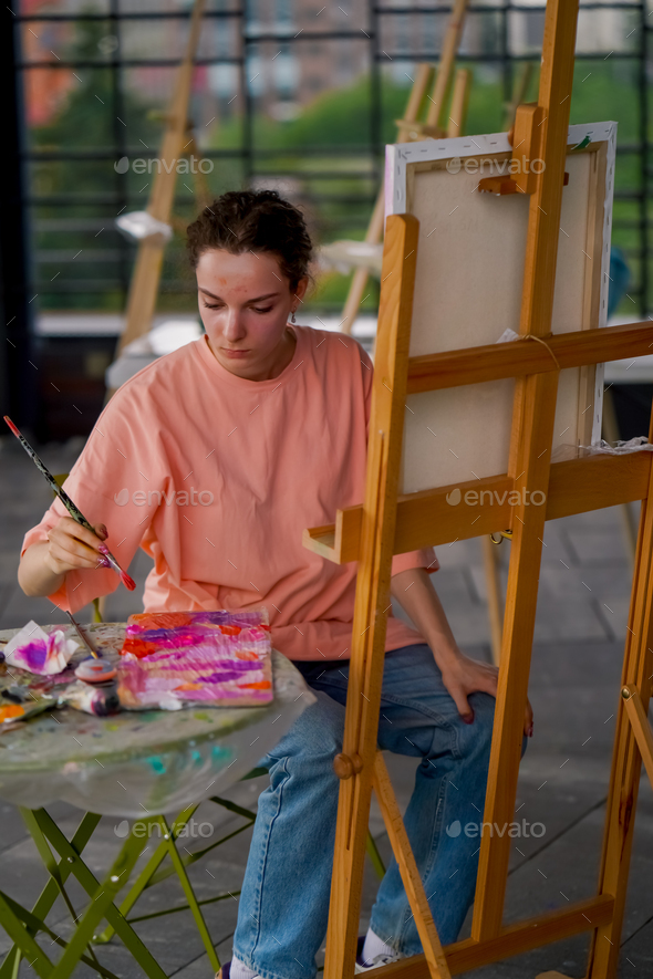 A girl artist with problem skin brushes paint from a painting palette ...
