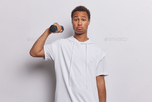 Puzzled confused dark skinned man lifts dumbbell trains biceps ...