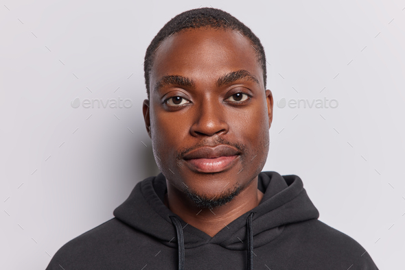 Portrait of serious dark skinned man looks directly at camera has self ...
