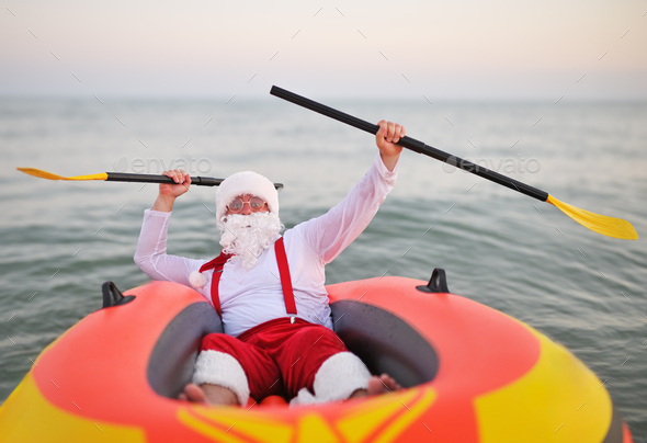 Santa in red suspenders floats on an inflatable boat against the ...
