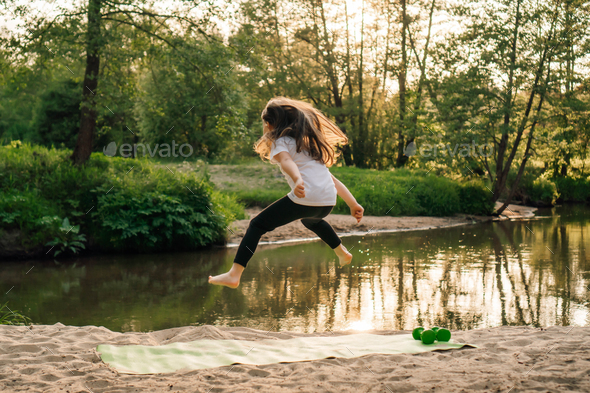 Active little athlete with long hair jumping high on sporty rug on ...