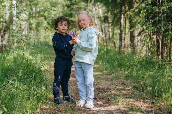 Two children exchange wildflowers on a forest path, sharing a gentle ...