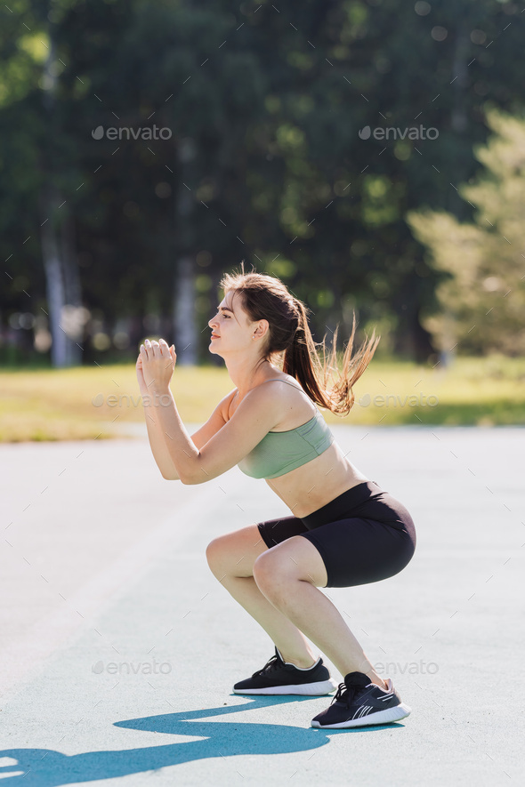f young student girl in sportswear making squats outdoors. Brunette ...