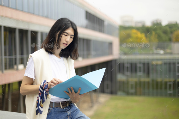 young chinese student reading some notes at the university entrance ...