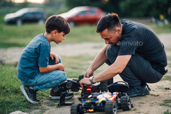 Boy watching his father fixing his overturned remote controlled toy car ...