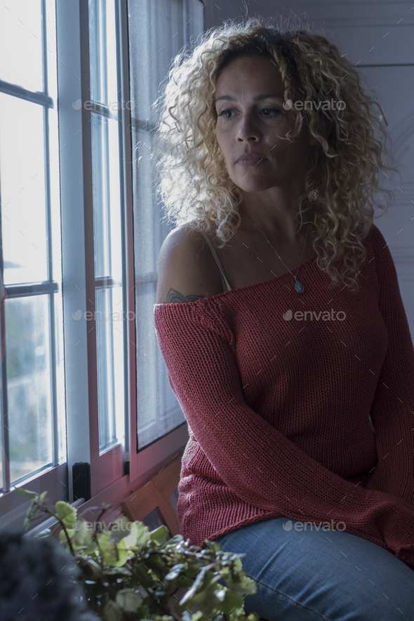 Sad woman alone at home looking outside the window - portrait of adult ...