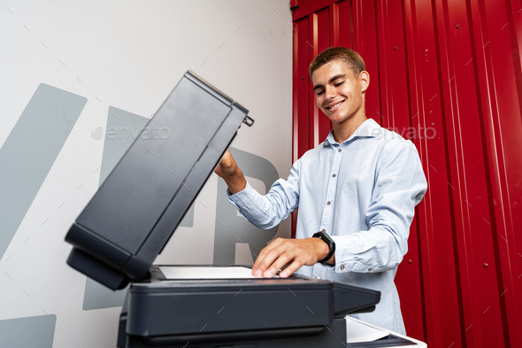 Positive young man using printer in the modern office Stock Photo by ...