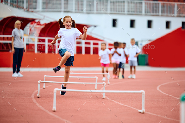 Happy girl jumping over obstacles while running at the stadium. Stock ...