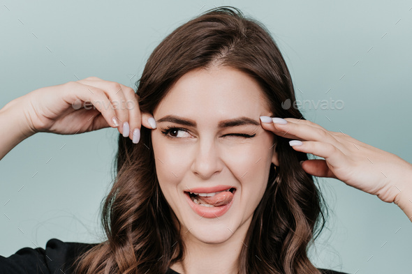 young brunette beautiful woman with wavy hair touching temples blinking ...