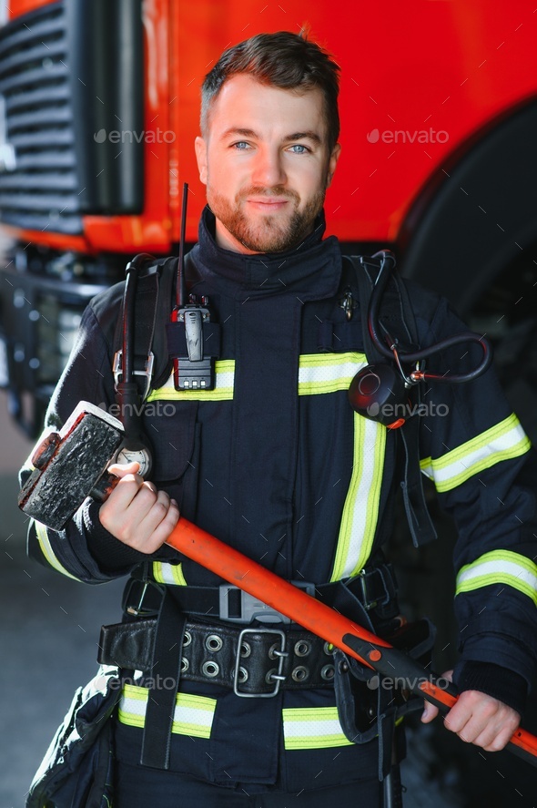 Photo of young fireman with sledgehammer in hands near fire engine ...