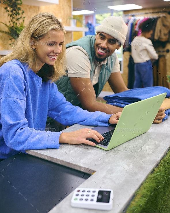 Male And Female Sales Assistant Working At Cash Desk With Laptop In Pop ...