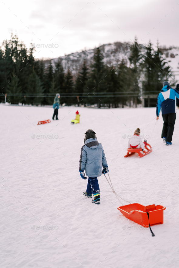 Child drags a sled on a rope walking up the hill towards people ...