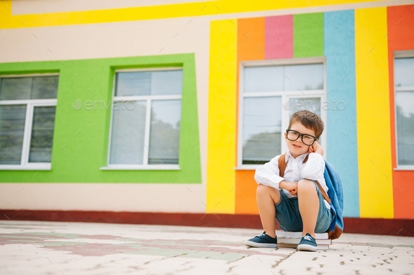 Sad little boy outside of school. Sad schoolboy with books near a ...
