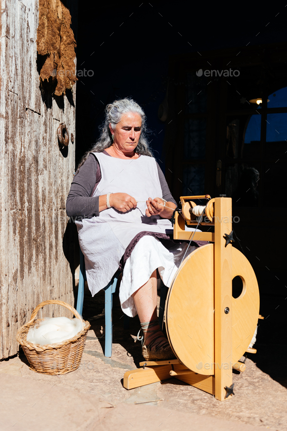 Full body of concentrated aged woman making thread with old wooden ...