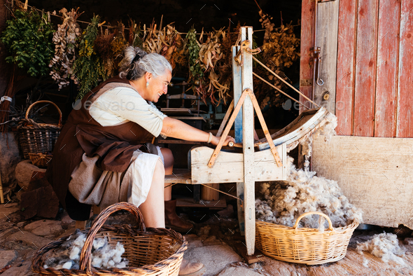 Cheerful senior female worker carding raw wool with old vintage wooden ...